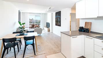 Uma cozinha moderna com armários brancos, um espaço de refeições com mesa e cadeiras, e vista para a cidade por grandes janelas.