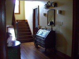 Uma escada que leva a um andar superior, um aparador de madeira com espelho e uma mesinha com objetos decorativos.
