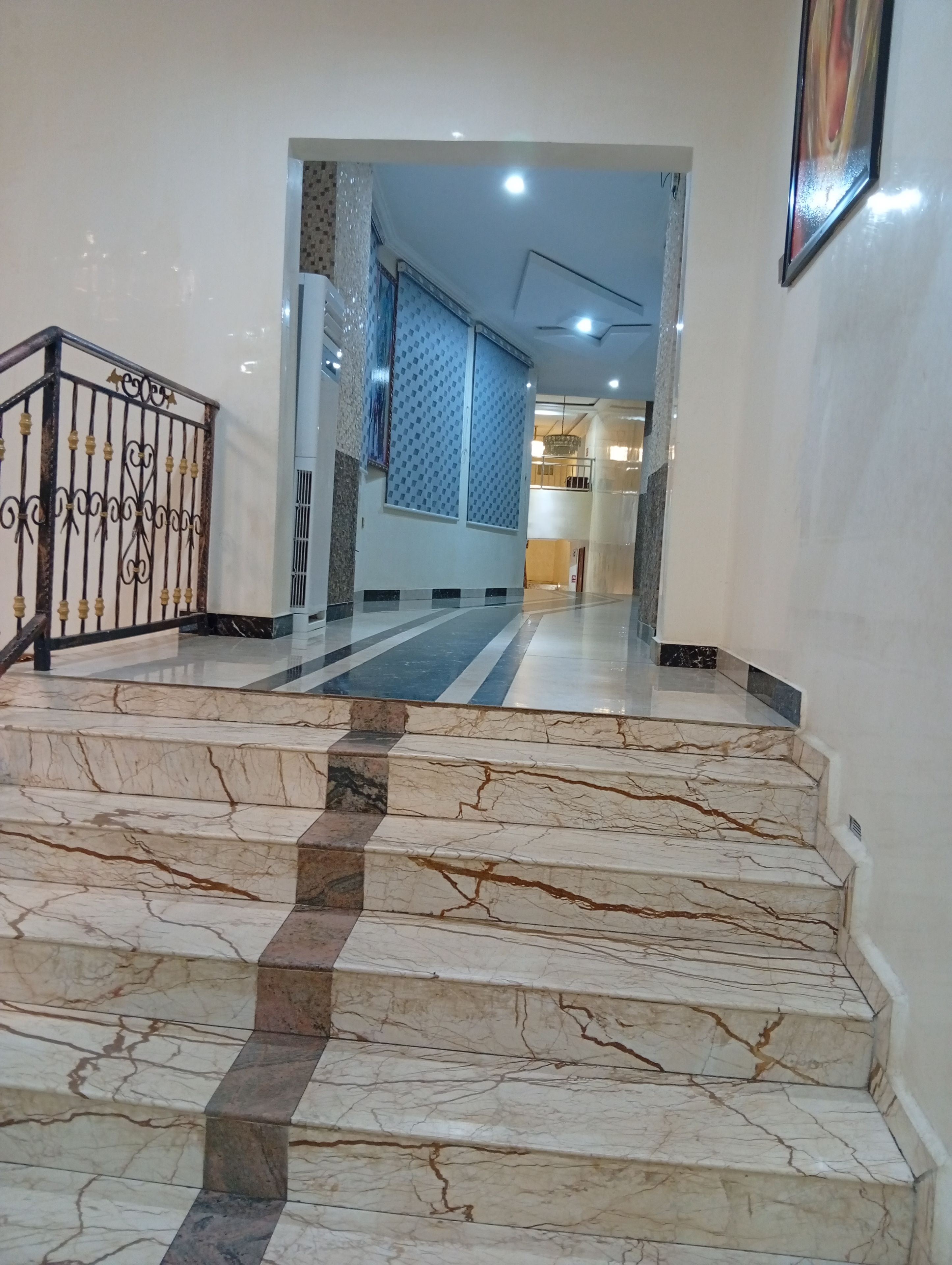 Uma escadaria de mármore leva a um quarto com cortina estampada e um candelabro.
