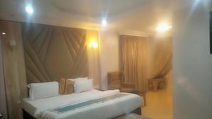 Quarto de hotel com uma cama grande, cabeceira com design geométrico, uma mesinha e uma cadeira.