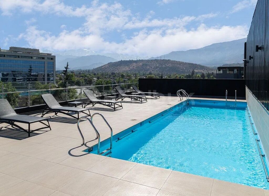 Uma piscina no terraço com espreguiçadeiras, vista desobstruída das montanhas e um edifício moderno ao fundo.