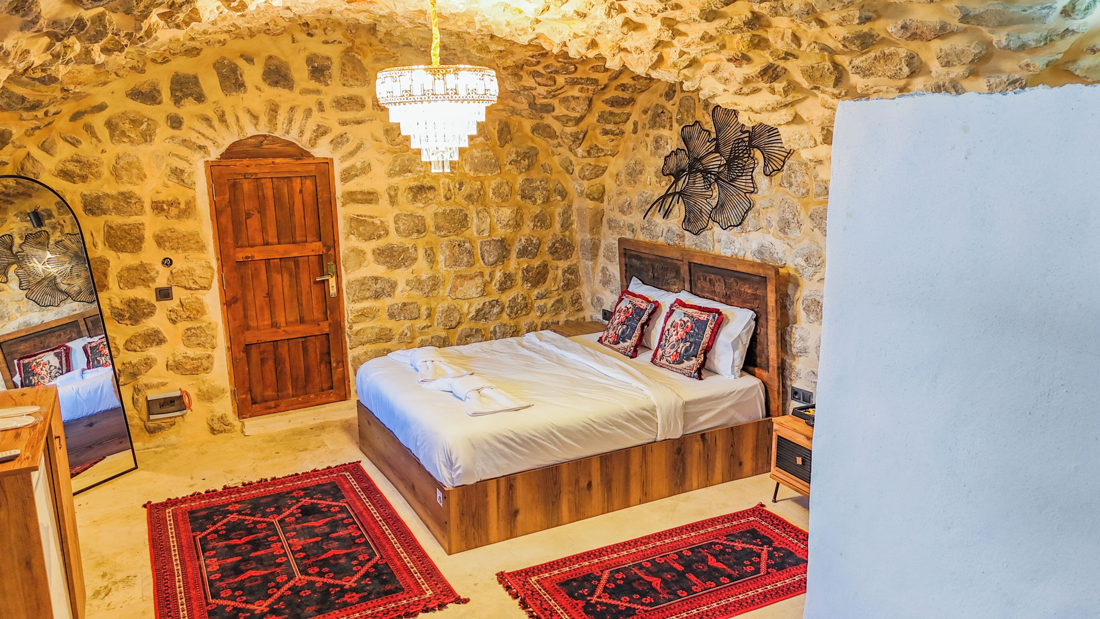 Quarto com paredes de pedra, uma cama de madeira, um candelabro e um espelho.