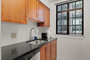 Uma cozinha com armários de madeira, uma pia de aço inoxidável e uma janela com vista para edifícios.