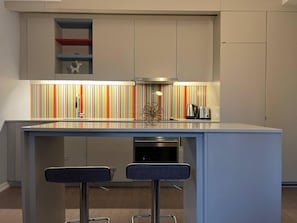 Cozinha moderna com ilha central, banquetas, painel colorido listrado e eletrodomésticos embutidos.