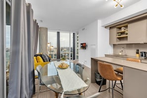 Apartamento moderno com área de jantar, cozinha e janelas amplas com vista para a cidade.