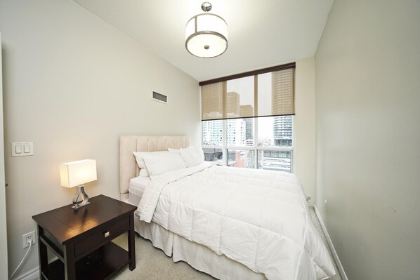 Quarto de hotel com cama, mesa de cabeceira, abajur e janela com persianas.