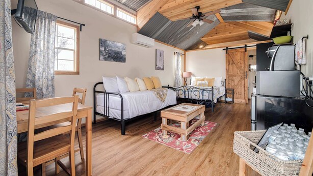 Um quarto acolhedor com uma cama, uma cadeira de madeira, uma mesa pequena e um frigorífico.