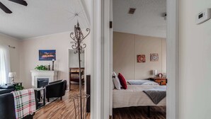 Um quarto com lareira, cama com almofadas, escrivaninha com abajur e um cabideiro.