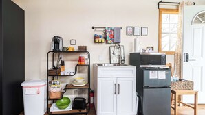 Uma cozinha compacta com geladeira branca, micro-ondas, pia e um pequeno armário com diversos utensílios de cozinha.