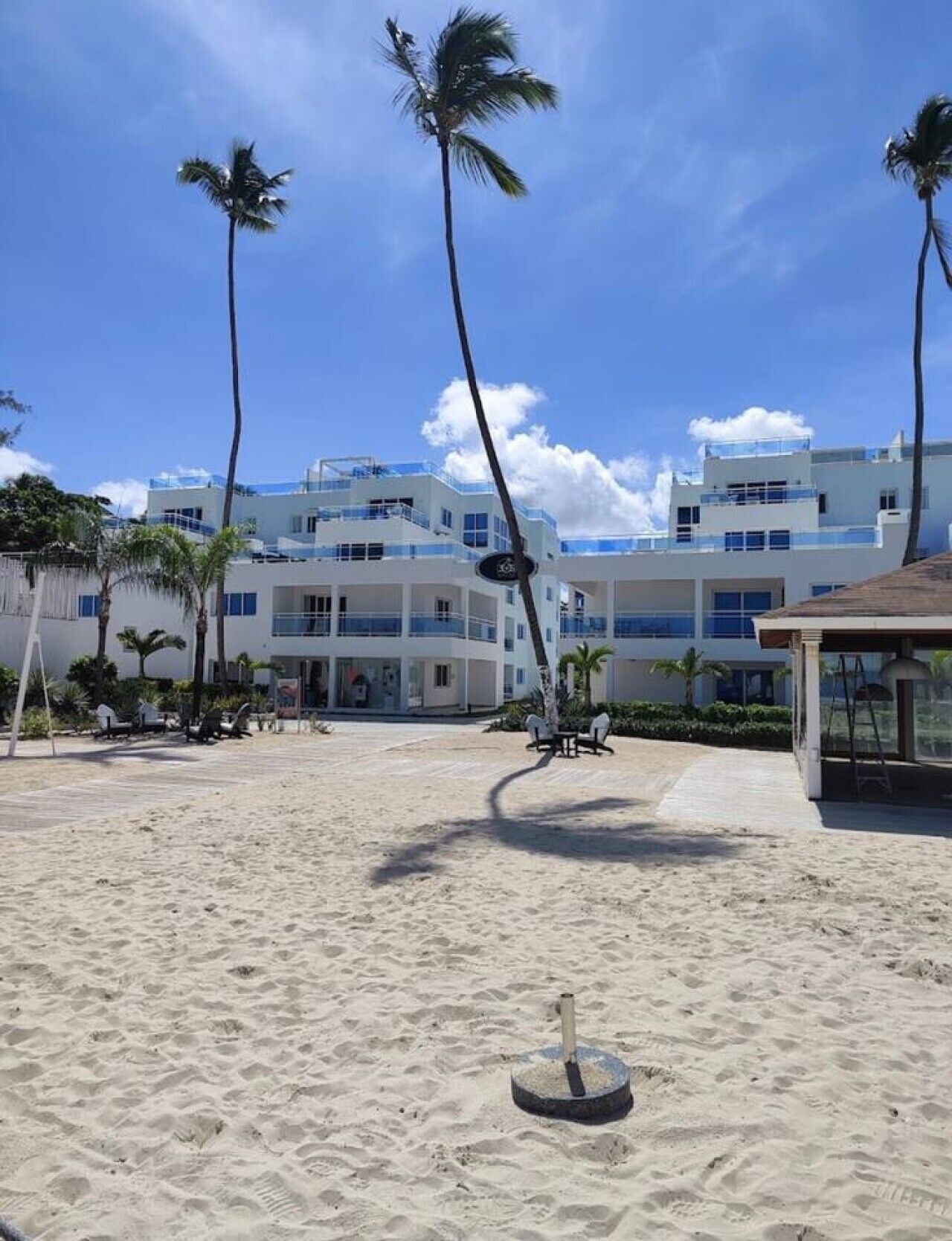 Hotel à beira-mar com vários andares, palmeiras e uma extensa área de praia arenosa.