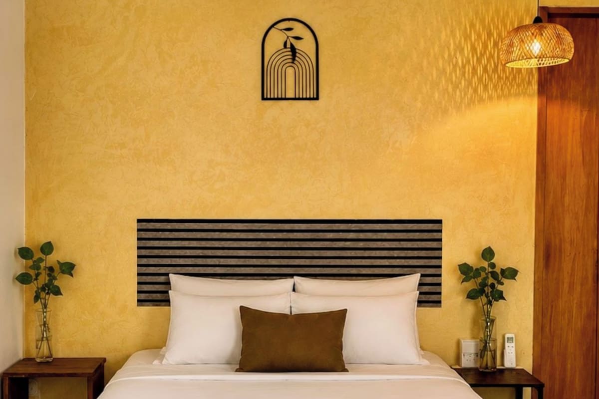 Uma cama com cabeceira, mesa de cabeceira com abajur e luminária na parede.