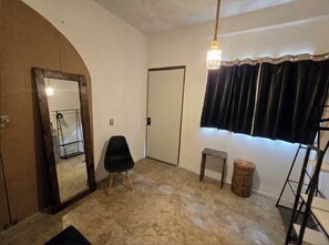 Um quarto com um espelho grande, uma porta, um pequeno banquinho, uma cesta de vime e um candeeiro suspenso.