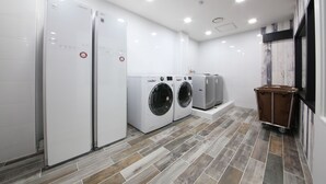 Uma lavanderia com um refrigerador branco, duas máquinas de lavar frontais e um carrinho.