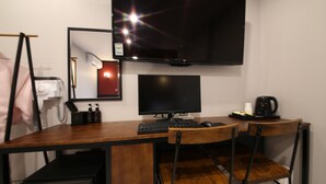 Quarto com escrivaninha, duas cadeiras, computador, monitor, televisão, cafeteira e espelho.
