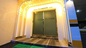 Entrada de hotel com uma placa em coreano, um par de portas duplas e uma rampa que leva até a entrada.