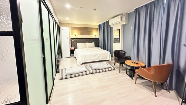 Quarto de hotel com cama, escrivaninha, cadeira e mesa pequena.