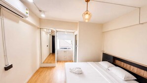 Quarto com piso de madeira, cama com roupa de cama branca, mesa de cabeceira e luminária pendente.