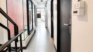 Corredor com corrimão, alarme de incêndio e porta com puxador.