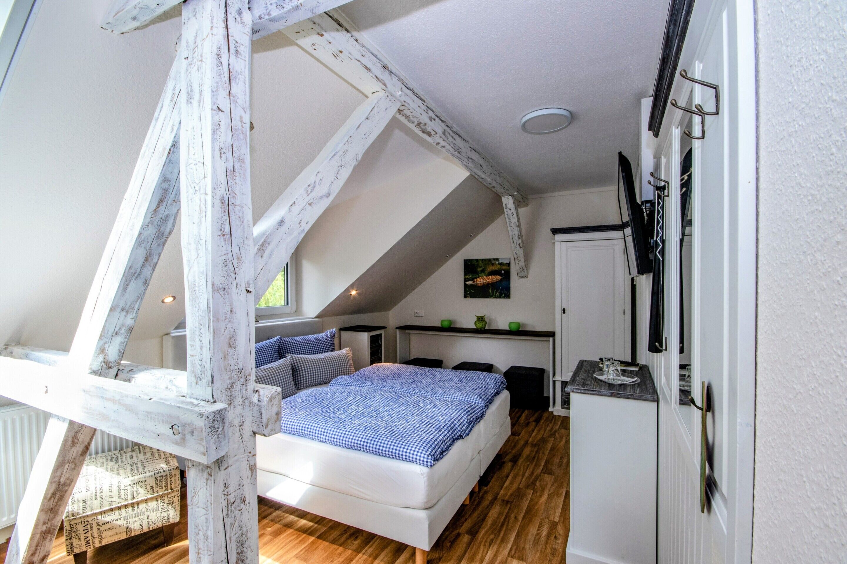 Um quarto no estilo loft com teto inclinado, uma cama com colcha xadrez, uma pequena escrivaninha e um radiador.