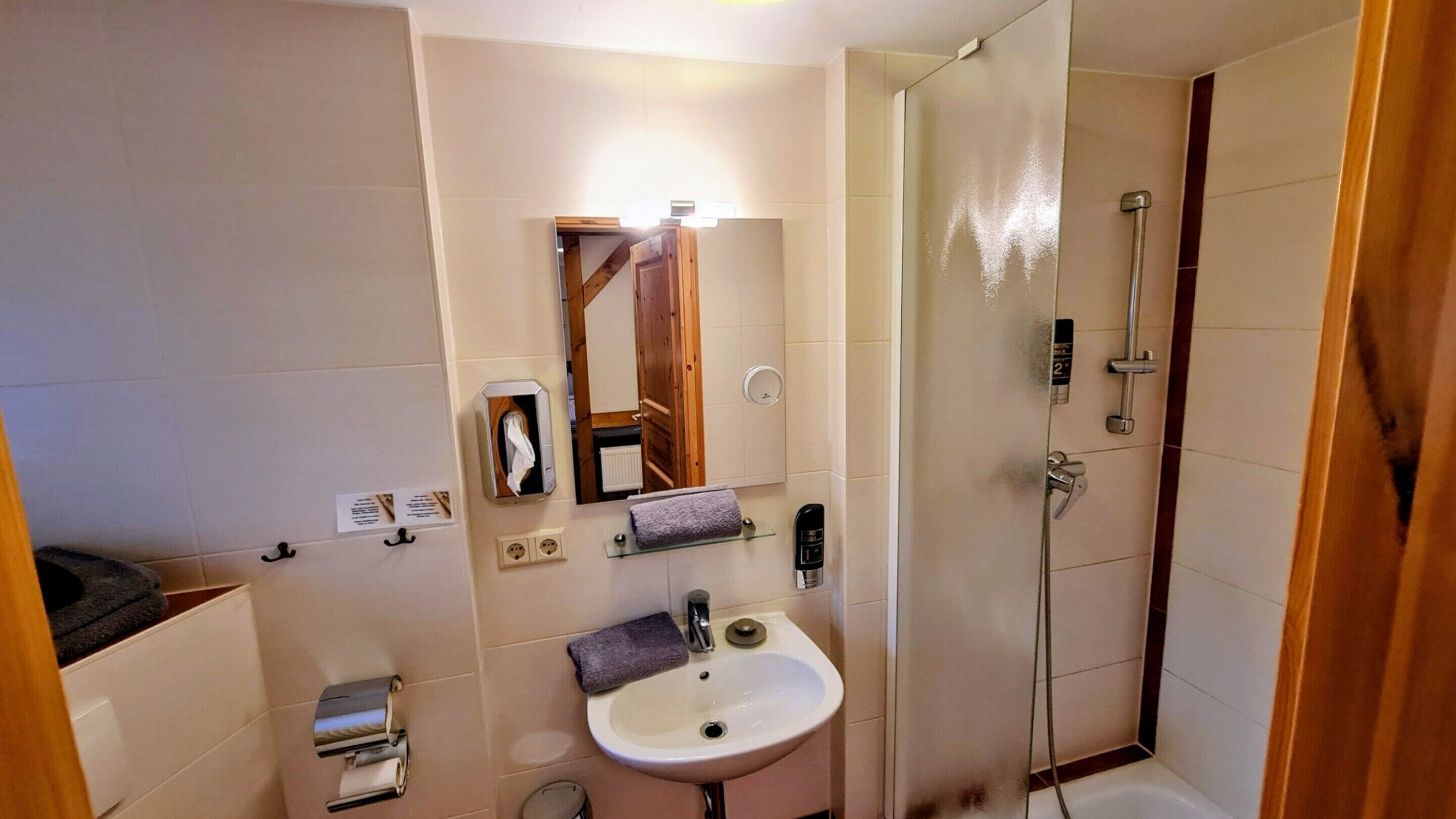 Uma casa de banho com chuveiro em cabine de vidro, pia, espelho e porta-toalhas.