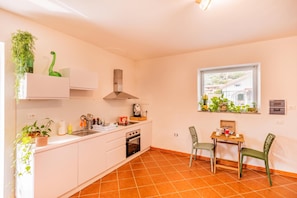 Uma cozinha compacta com armários brancos, fogão e janela com vista para uma casa.