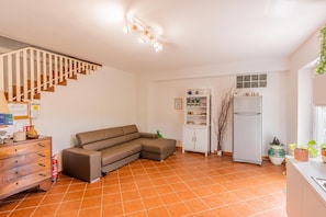 Uma sala de estar moderna com um sofá seccional marrom, um armário branco e uma cozinha com geladeira e mais um armário branco.