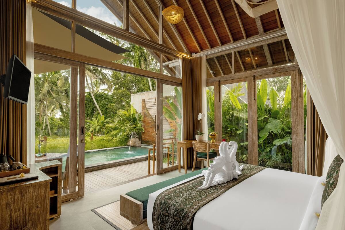 Quarto com uma cama grande, uma escrivaninha de madeira, televisão e vista para a piscina e jardim.