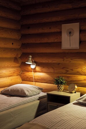Quarto de cabana de tronco com duas camas, um abajur, um relógio e um quadro na parede.