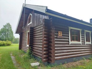Uma cabana de toras com uma placa com o número 2, uma janela com persianas e um pequeno alpendre.