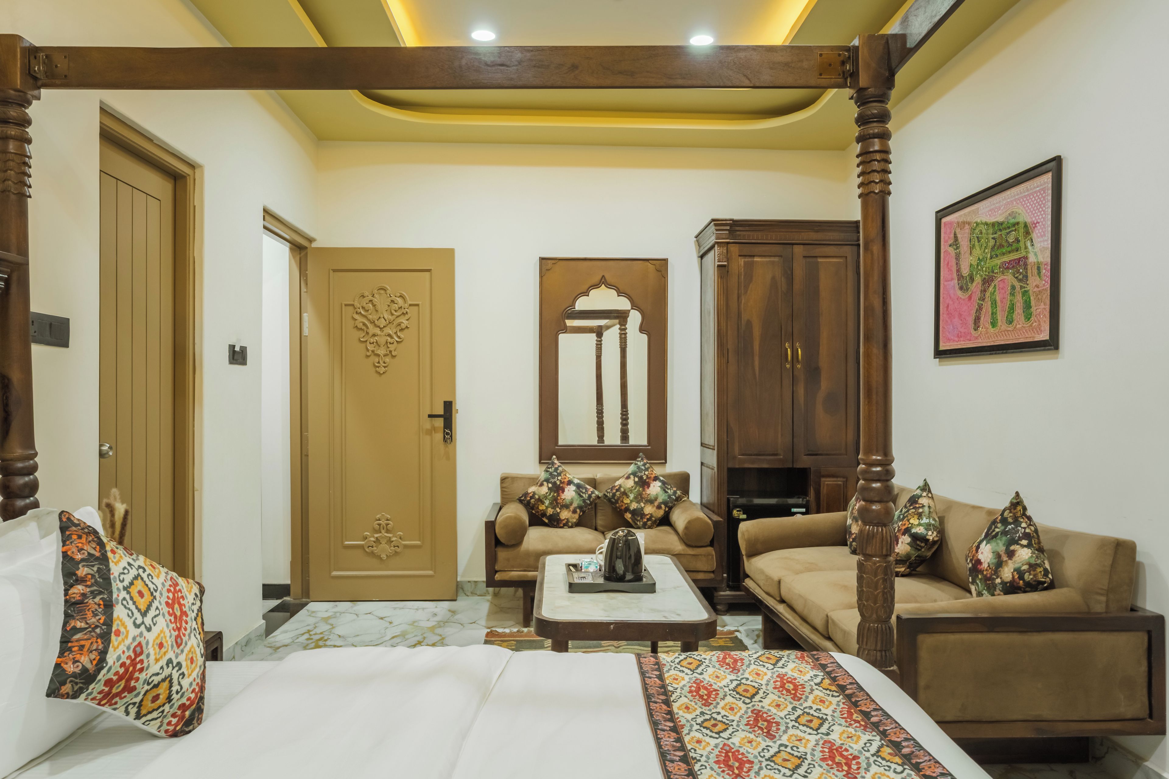 Quarto de hotel com cama, dois sofás, mesa de centro, televisão e porta com puxador decorativo.
