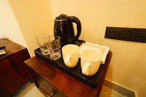 Uma pequena cozinha com uma cafeteira, duas chávenas brancas e dois copos sobre um balcão de madeira.