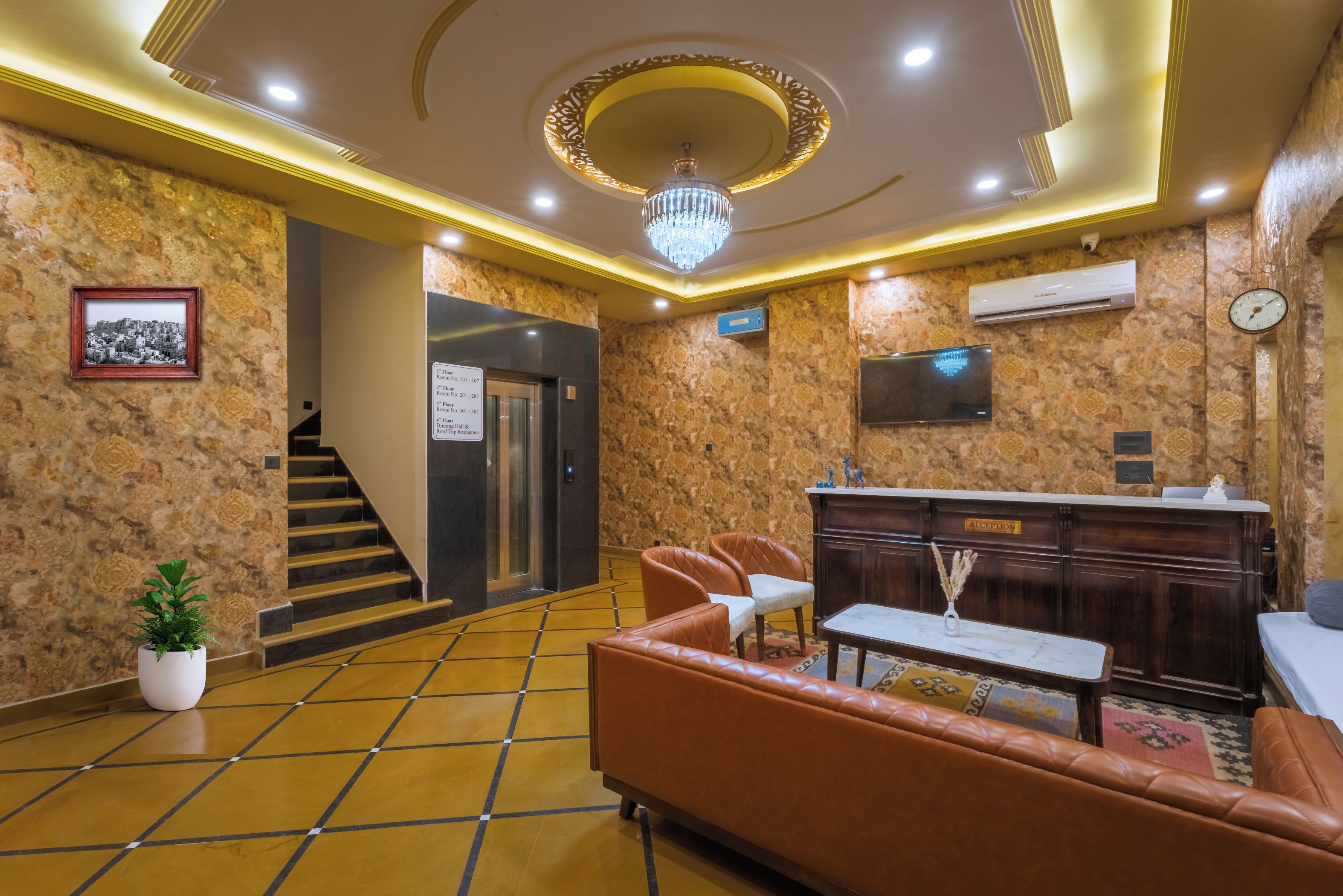 Um saguão de hotel com balcão de recepção, sofás de couro, um candelabro, uma escada e um relógio fixado na parede.