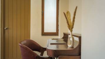 Quarto com porta de madeira, uma escrivaninha com um vaso de capim-do-campo e uma cadeira.