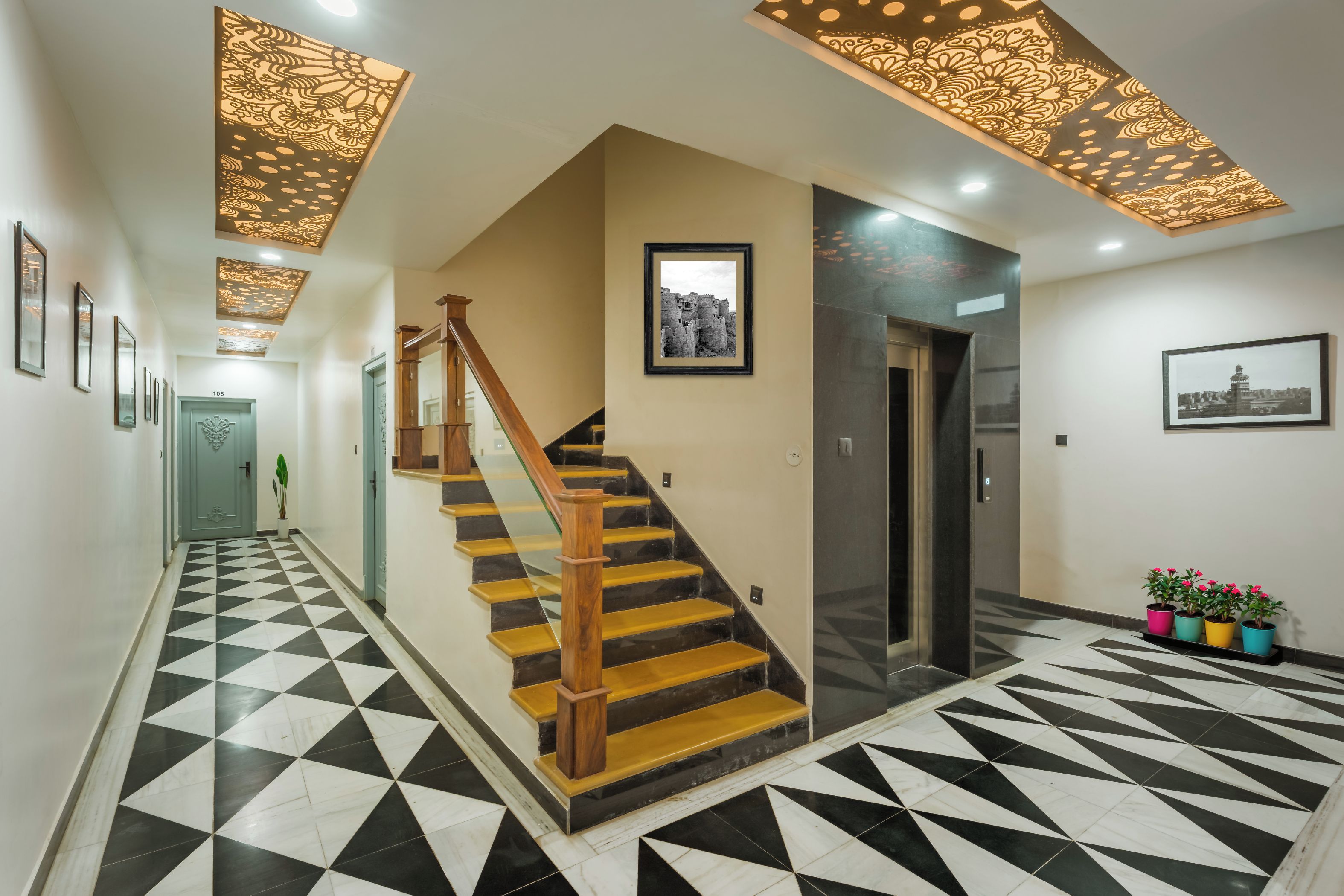 Um saguão de hotel com piso xadrez preto e branco, escada de madeira e elevador moderno.