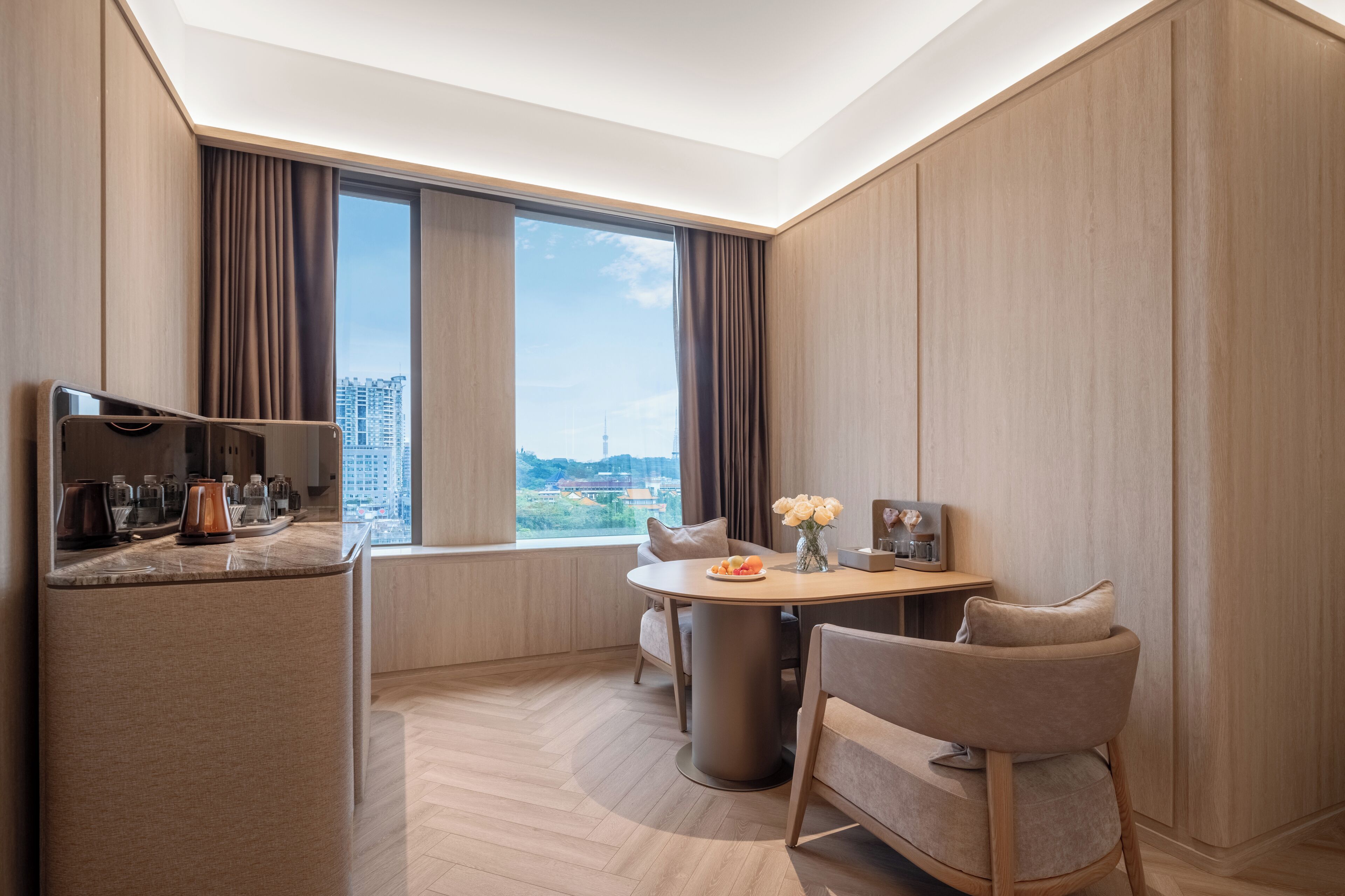 Quarto de hotel moderno com área de refeições, bancada de cozinha e uma grande janela com vista para a cidade.