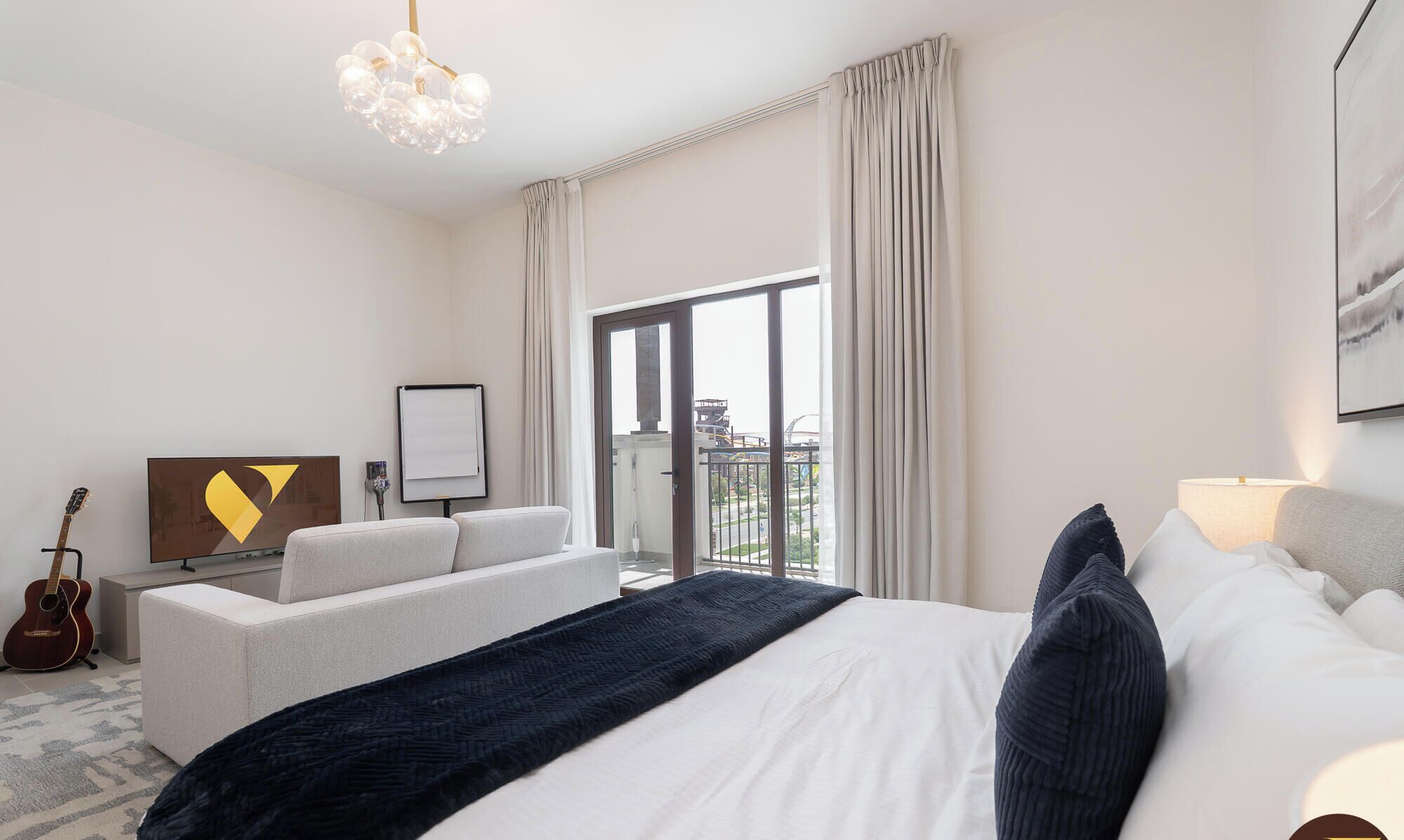 Quarto de hotel com cama, sofá, guitarra, televisão e varanda com cortinas.