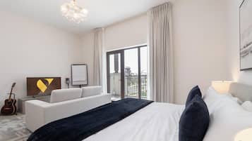 Quarto de hotel com cama, sofá, guitarra, televisão e varanda com cortinas.