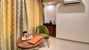 Um quarto com uma mesa redonda de madeira, uma cadeira verde, uma garrafa de água, uma chaleira e uma cafeteira sobre a mesa.