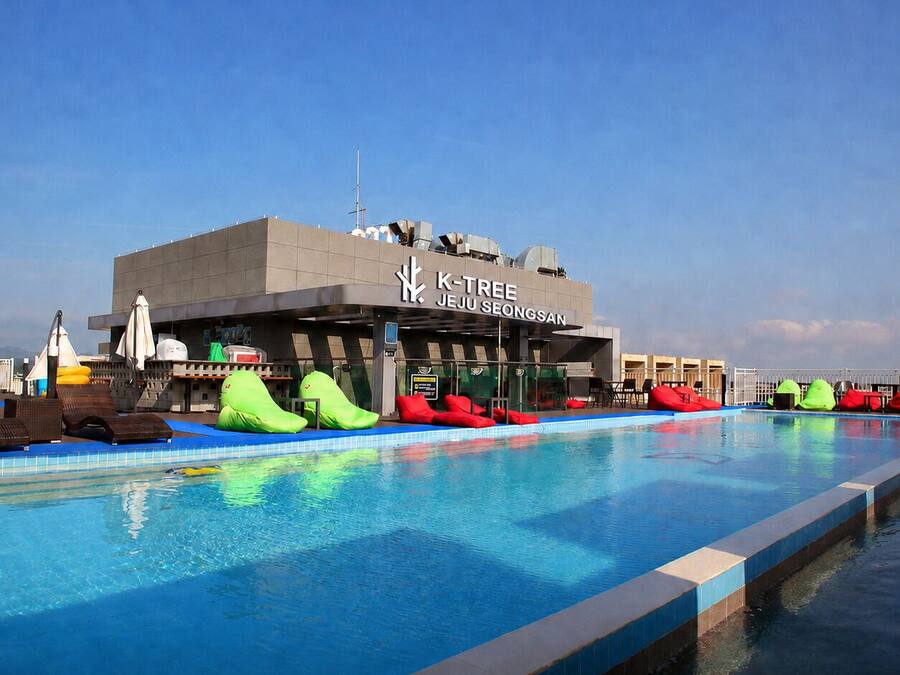 Uma piscina com espreguiçadeiras e um edifício com a inscrição 'K-Tree Jeju Seongsan'.