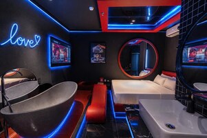Um banheiro moderno com uma banheira grande, um espelho redondo e uma luminária neon.