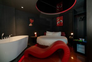Quarto moderno com uma cama grande, uma cadeira vermelha, banheira e obras de arte nas paredes.