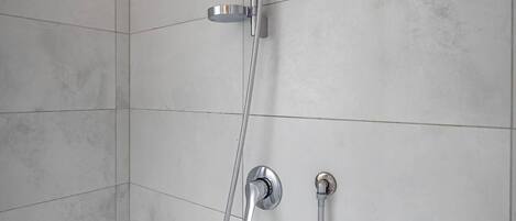 Um chuveiro com um chuveiro manual e uma torneira fixa num banheiro revestido com azulejos.