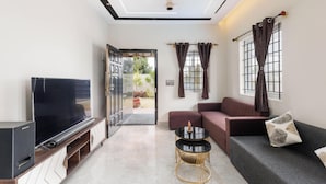 Uma sala de estar com televisão de tela plana, um sofá, uma mesa de centro e uma porta que dá para um jardim.