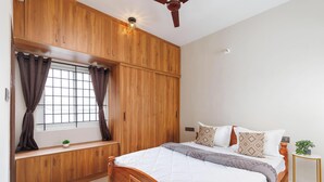 Quarto com cama de madeira, janela com cortinas, ventilador de teto e mesa de cabeceira com uma planta.