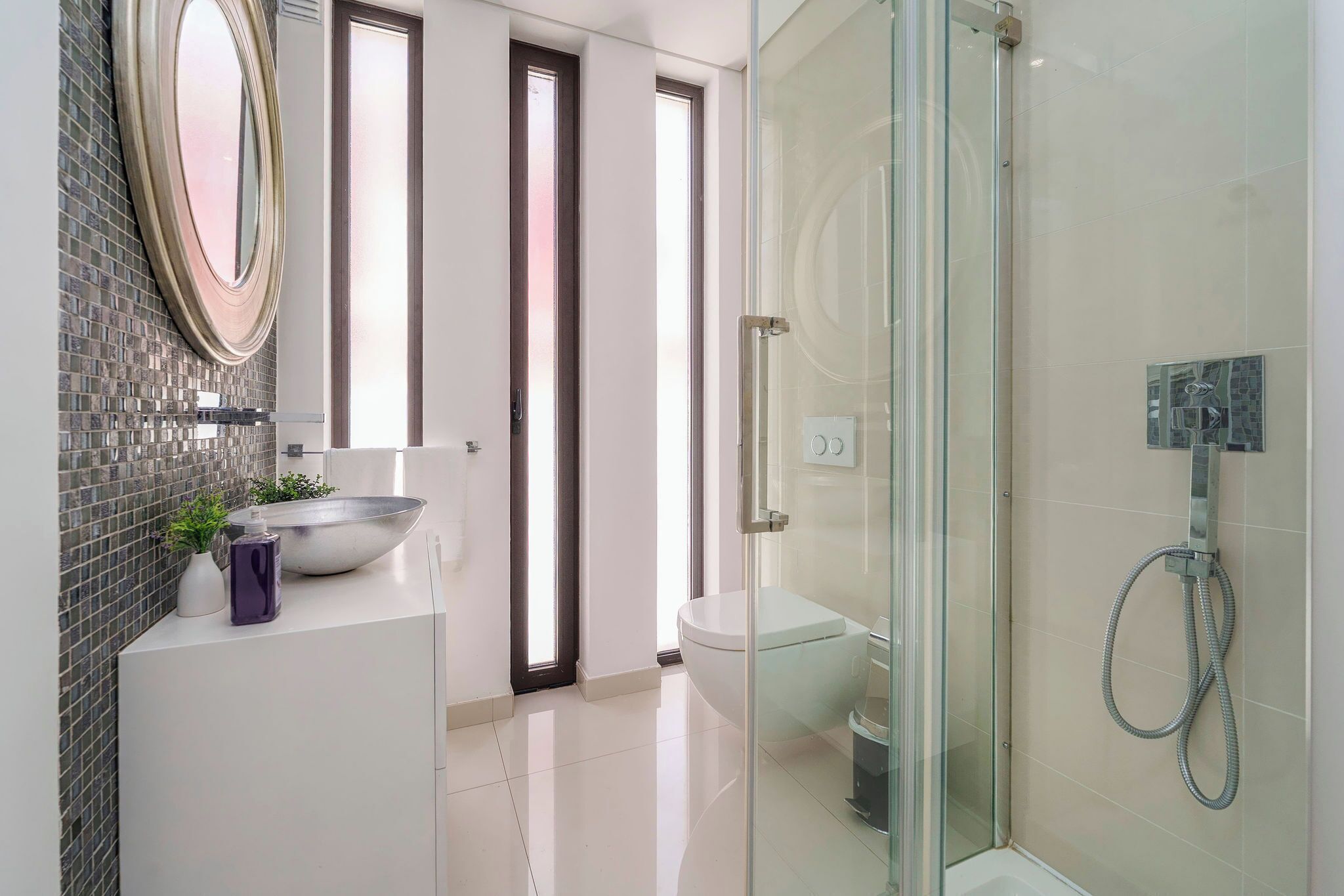 Uma casa de banho moderna com cabine de duche em vidro, um espelho grande e uma pia branca.