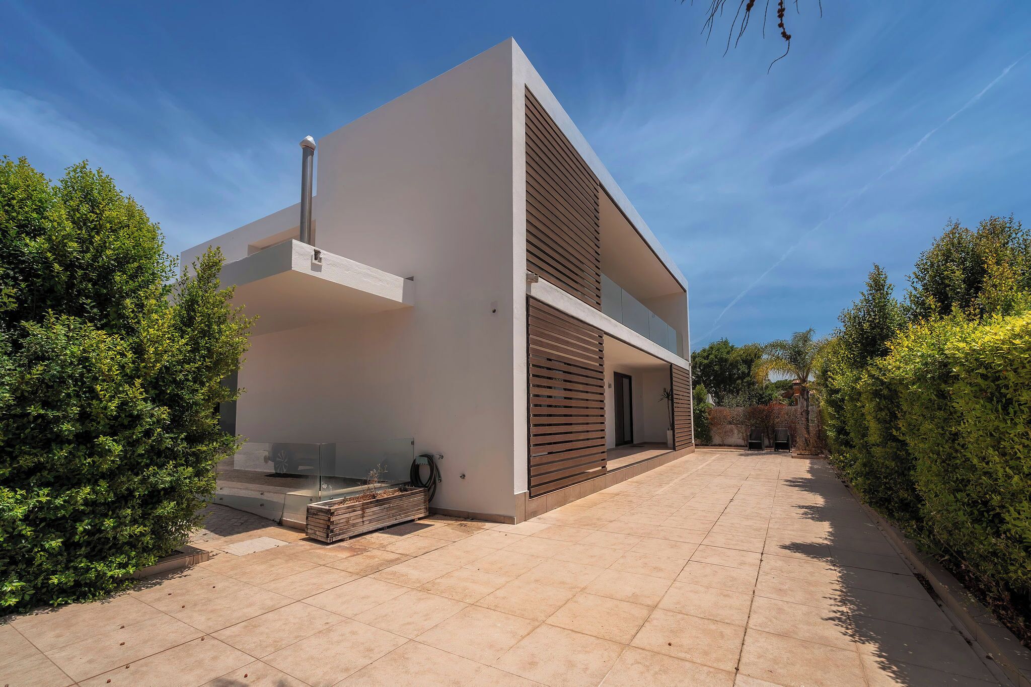 Uma casa moderna de dois andares com telhado plano, varanda e entrada com calçada.