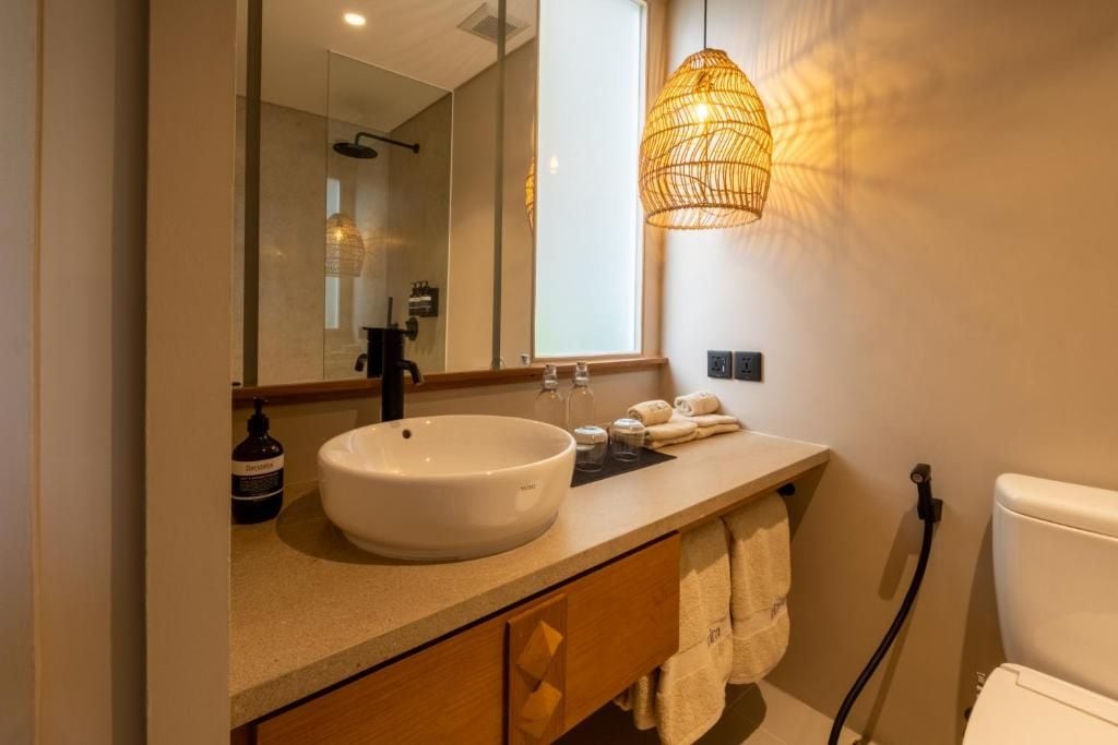 Casa de banho com um espelho grande, uma pia branca, um porta-toalhas e um candeeiro pendente.