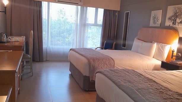 Quarto de hotel com duas camas, uma escrivaninha, uma cadeira e uma janela com cortinas.