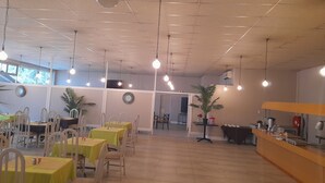 Uma área de refeições com mesas, cadeiras, um balcão e luminárias pendentes.