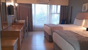 Quarto de hotel com cama, escrivaninha, cadeira, espelho e janela.